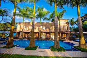 Resort com piscina, palmeiras e um edifício com várias janelas e sacadas.