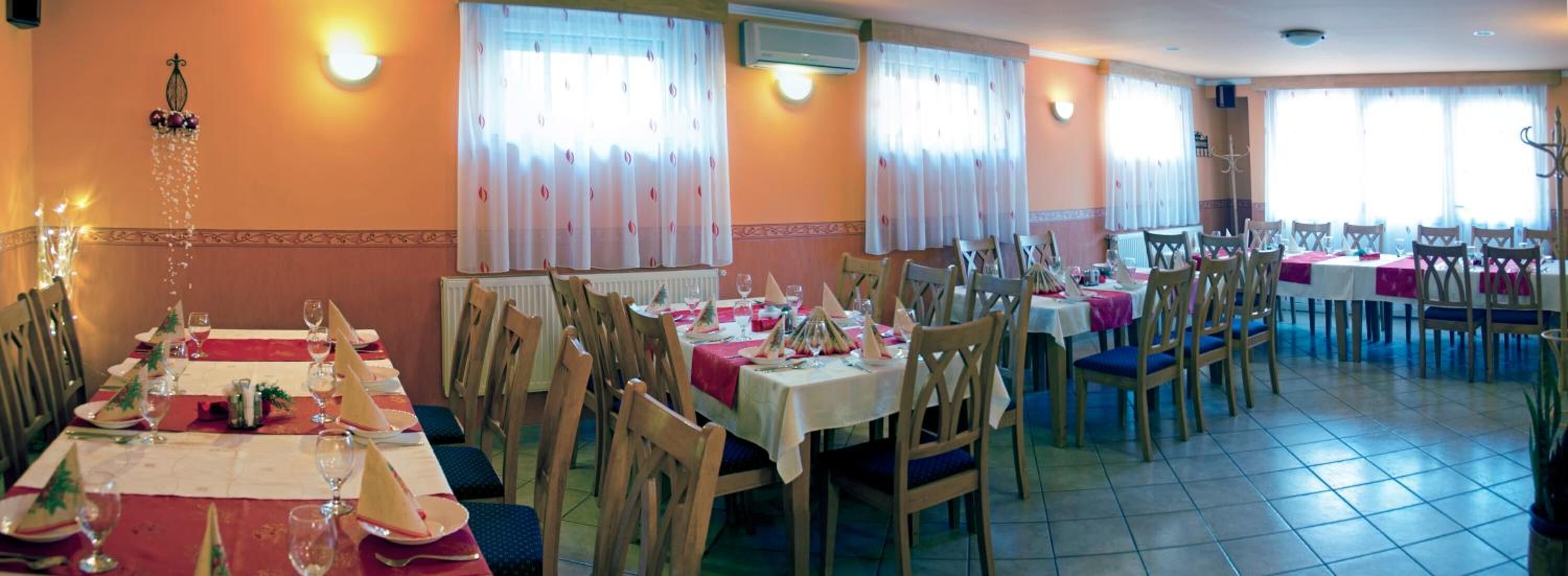 Um restaurante com várias mesas preparadas para refeições, cadeiras de madeira e piso de azulejos.