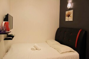 Uma cama bem arrumada com uma toalha enrolada, uma mesa de cabeceira com abajur e um quadro pendurado na parede.