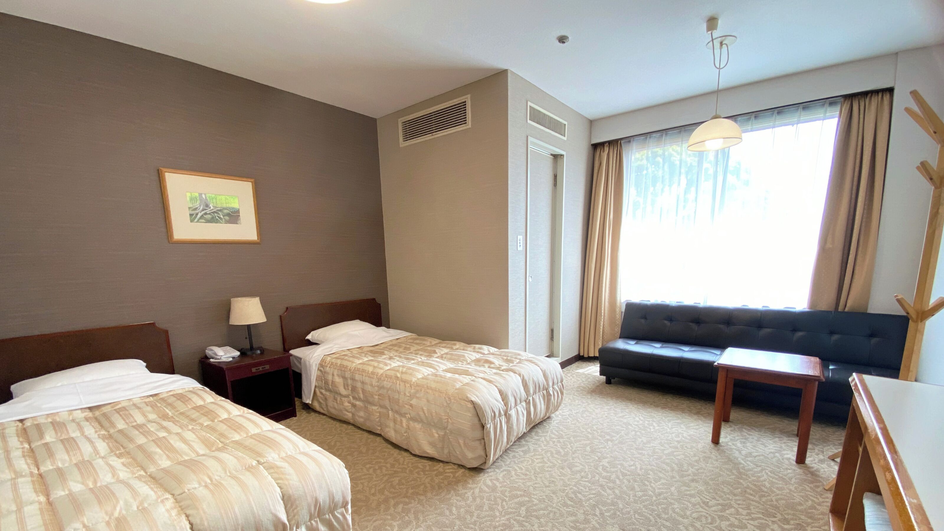 Quarto de hotel com duas camas, um sofá, uma pequena mesa, uma lâmpada, um telefone e um quadro na parede.