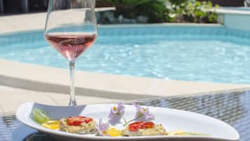Mesa de jantar com prato de comida e copo de vinho perto de uma piscina.