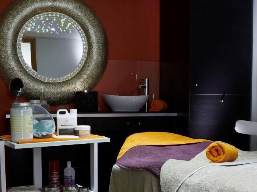 Quarto de hotel com cama, mesa de cabeceira com artigos de higiene, espelho e pia.