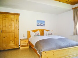 Um quarto com uma cama de madeira, uma mesa de cabeceira, um guarda-roupa de madeira e uma pintura de montanhas na parede.