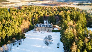 Um edifício grande e histórico cercado por uma floresta densa e terreno coberto de neve.