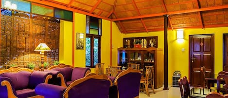 Quarto com sofás roxos, cadeiras de madeira, uma mesa de jantar e um ventilador de teto.