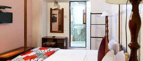 Quarto de hotel com cama, mesa de cabeceira, abajur e vista para o banheiro por uma porta aberta.