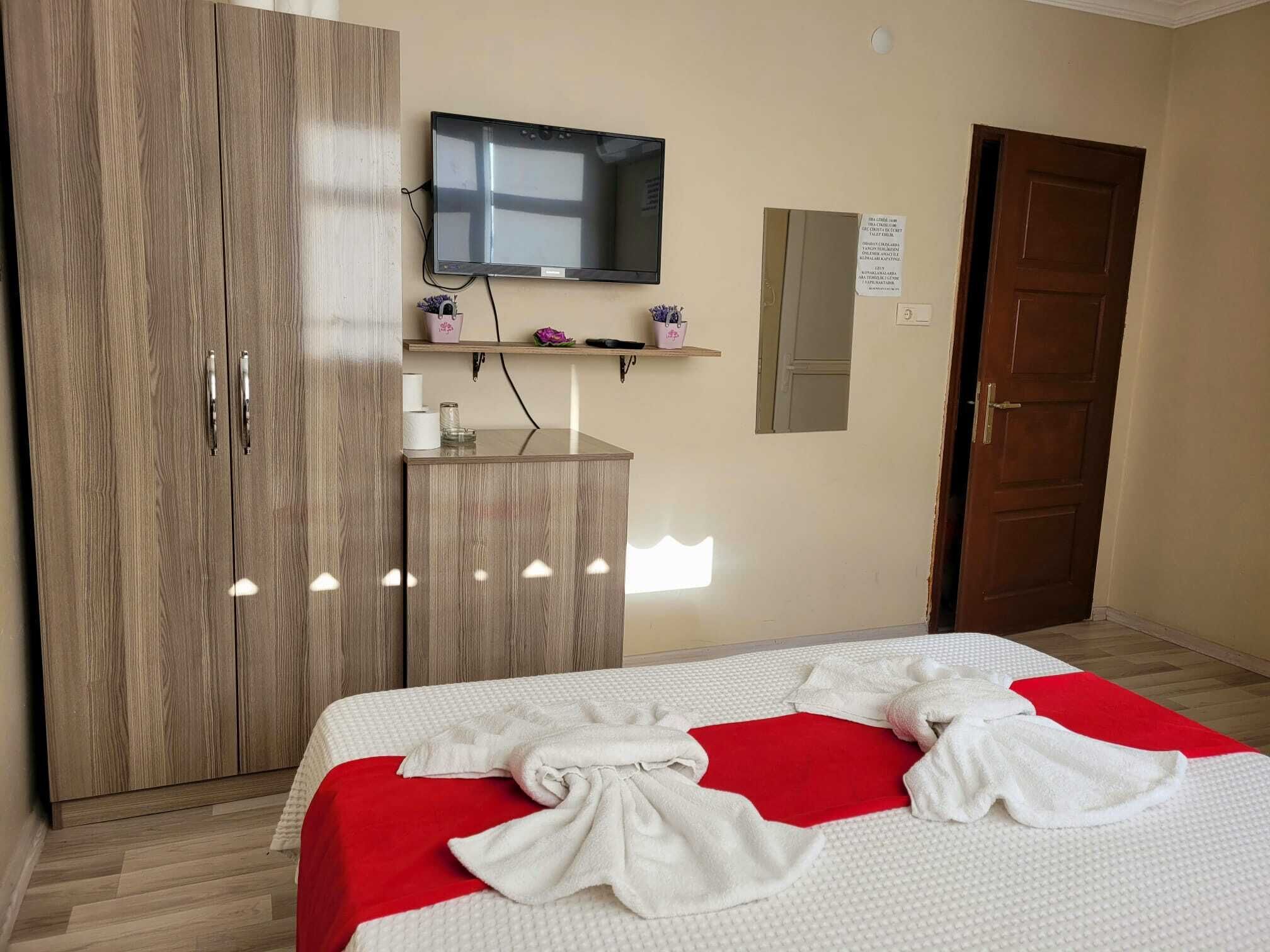 Quarto de hotel com uma cama, televisão, guarda-roupa e um pequeno armário com artigos de higiene pessoal.