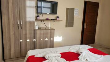 Quarto de hotel com uma cama, televisão, guarda-roupa e um pequeno armário com artigos de higiene pessoal.