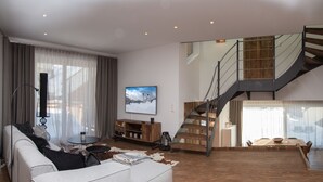 Uma sala de estar moderna com um sofá, uma mesa de centro, uma televisão e uma escada que leva a um andar superior.
