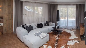 Uma sala de estar moderna com um sofá seccional, uma mesa de centro redonda e uma janela grande com cortinas leves.