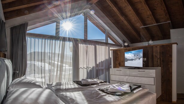 Quarto com uma janela grande, televisão e teto de madeira.