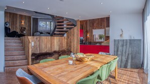 Uma cozinha moderna com bancada vermelha, escada de madeira e área de jantar com mesa e cadeiras verdes.