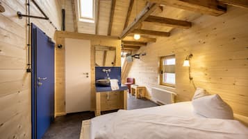 Um quarto de madeira com uma cama, uma porta azul, uma pia e uma janela.