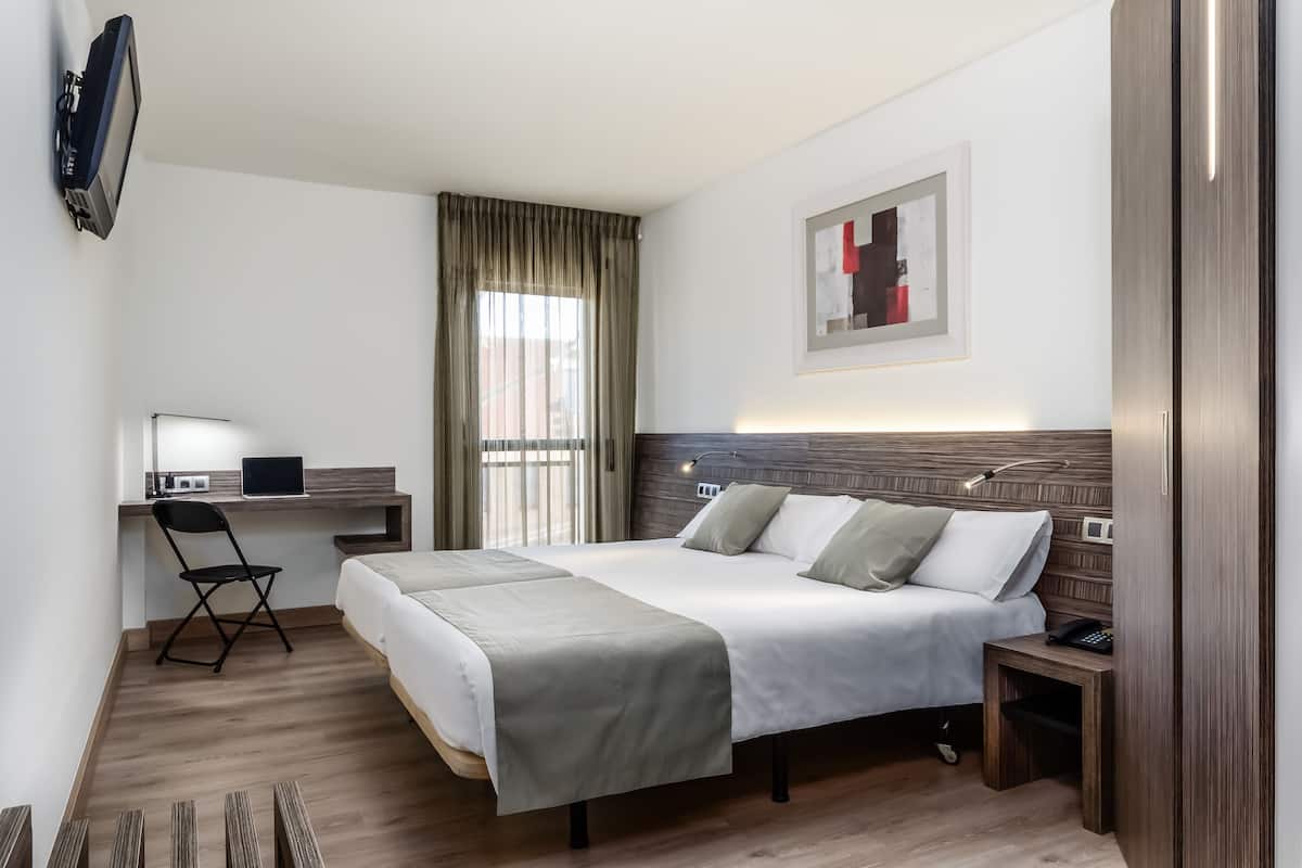 Quarto de hotel com cama, escrivaninha, cadeira e um quadro na parede.