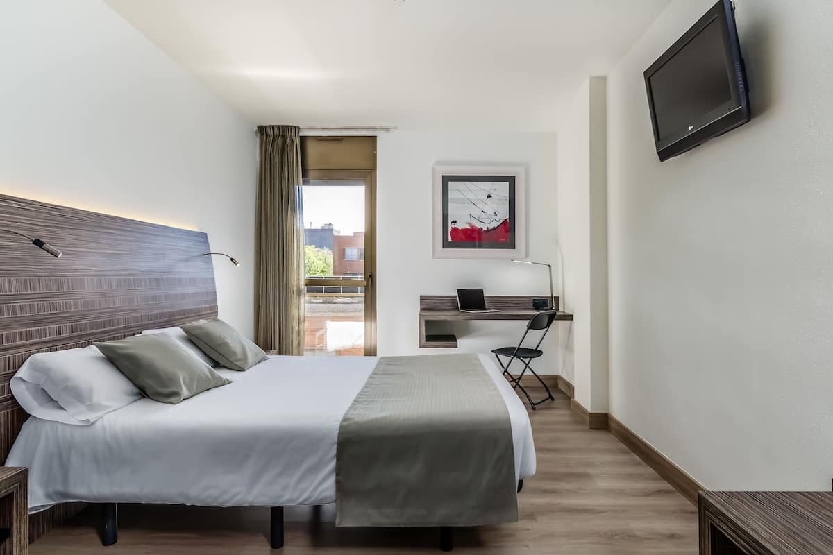 Quarto de hotel com cama, escrivaninha, cadeira, televisão e obras de arte.