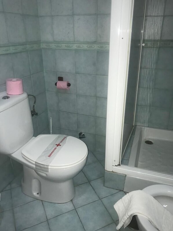 Uma casa de banho com sanita, chuveiro e lavatório.