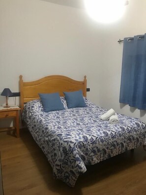 Uma cama com colcha florida, duas almofadas e uma toalha enrolada.