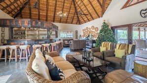 Uma área de estar ampla, com pé direito alto e teto de palha, incluindo um bar com banquetas e uma árvore de Natal.