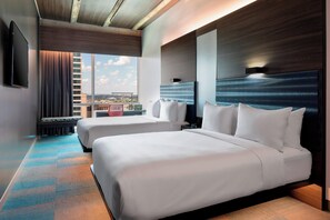 Quarto de hotel com duas camas, uma janela grande com vista para a cidade, uma televisão de tela plana e design moderno.
