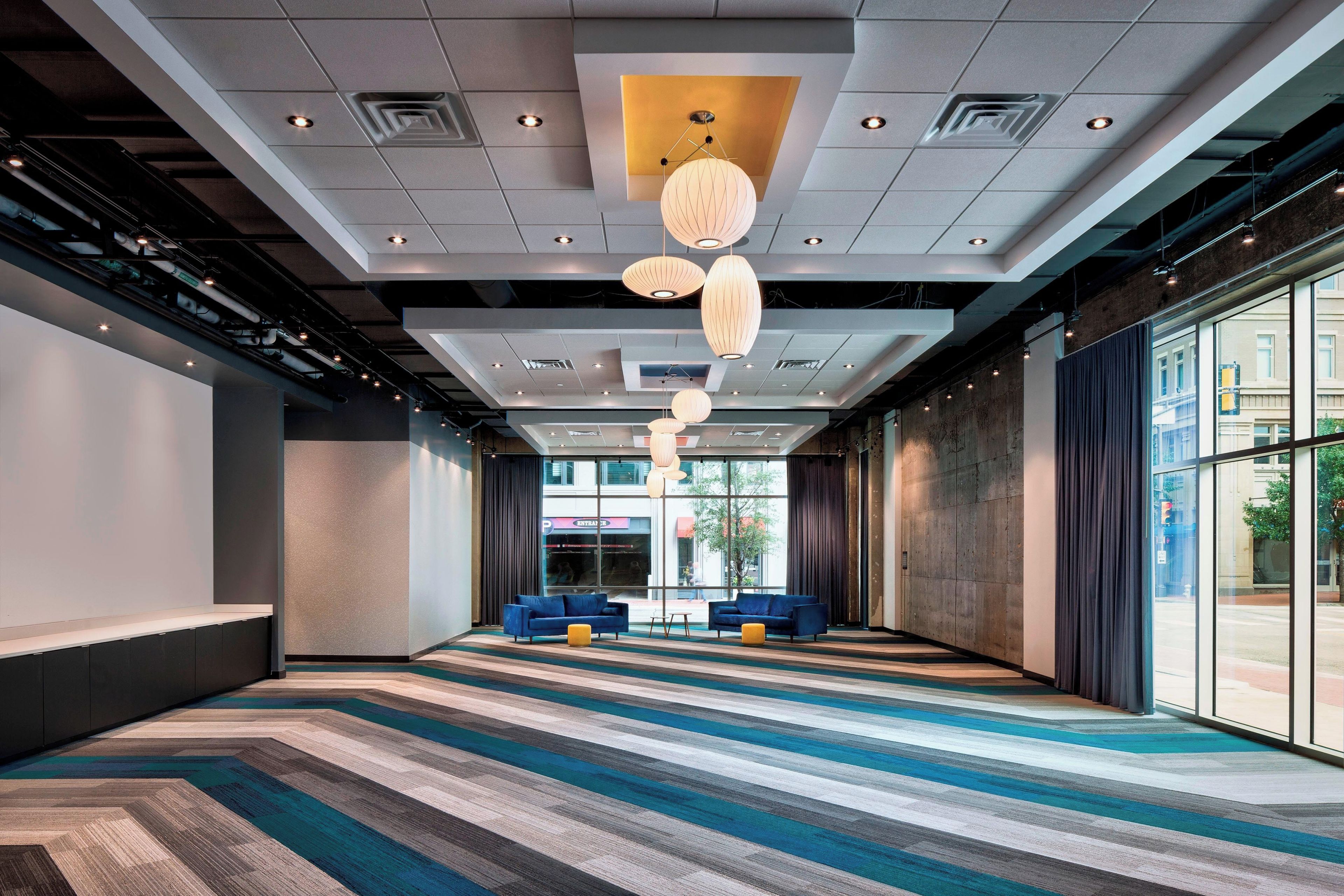 Um hall de hotel espaçoso com design moderno, apresentando um balcão de atendimento extenso, amplas janelas e um carpete estampado.
