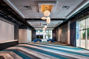 Um hall de hotel espaçoso com design moderno, apresentando um balcão de atendimento extenso, amplas janelas e um carpete estampado.