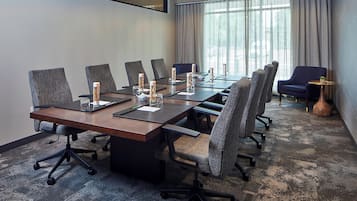 Uma sala de conferência com uma mesa comprida, várias cadeiras e uma mesinha lateral com uma planta.