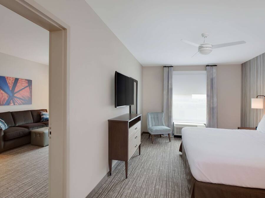 Quarto de hotel com cama, televisão, escrivaninha, cadeira e janela com cortinas.