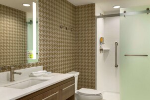 Um banheiro com parede estampada em xadrez houndstooth, pia branca com torneira moderna, vaso sanitário e box de vidro com chuveiro manual.