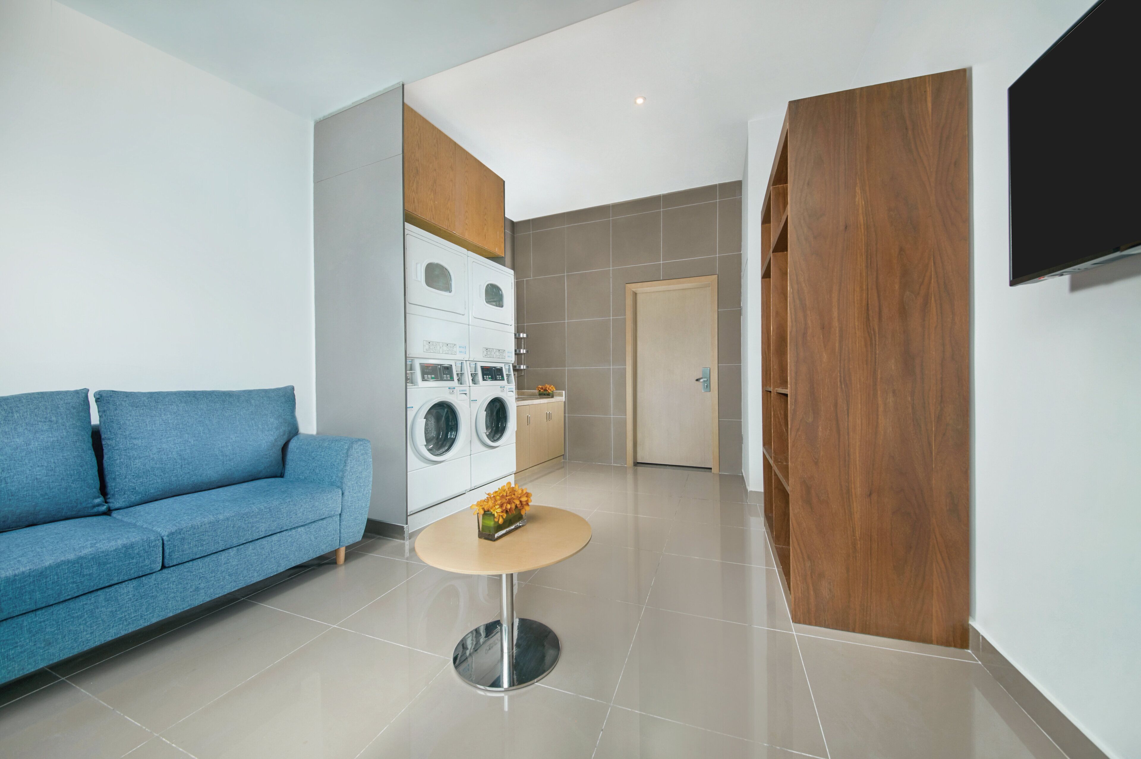 Uma sala de estar moderna com um sofá azul, uma mesa de centro com flores, uma máquina de lavar e uma porta de madeira.
