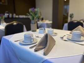 Uma mesa de jantar bem posta, com toalhas brancas, pratos, chávenas e talheres.