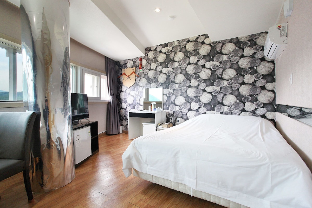 Quarto de hotel com cama, escrivaninha, televisão e parede com padrão de pedra.