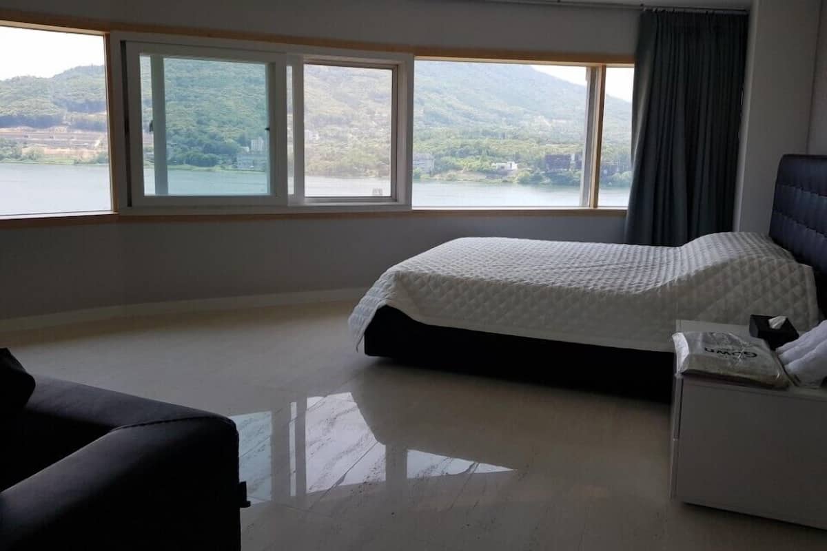 Quarto com cama, mesa de cabeceira e vista para um lago e montanhas.