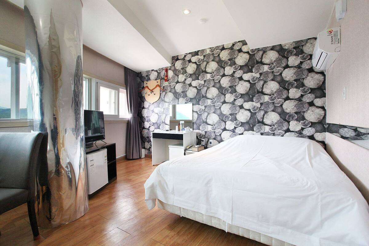Quarto com cama, escrivaninha, televisão e parede com padrão de pedra.