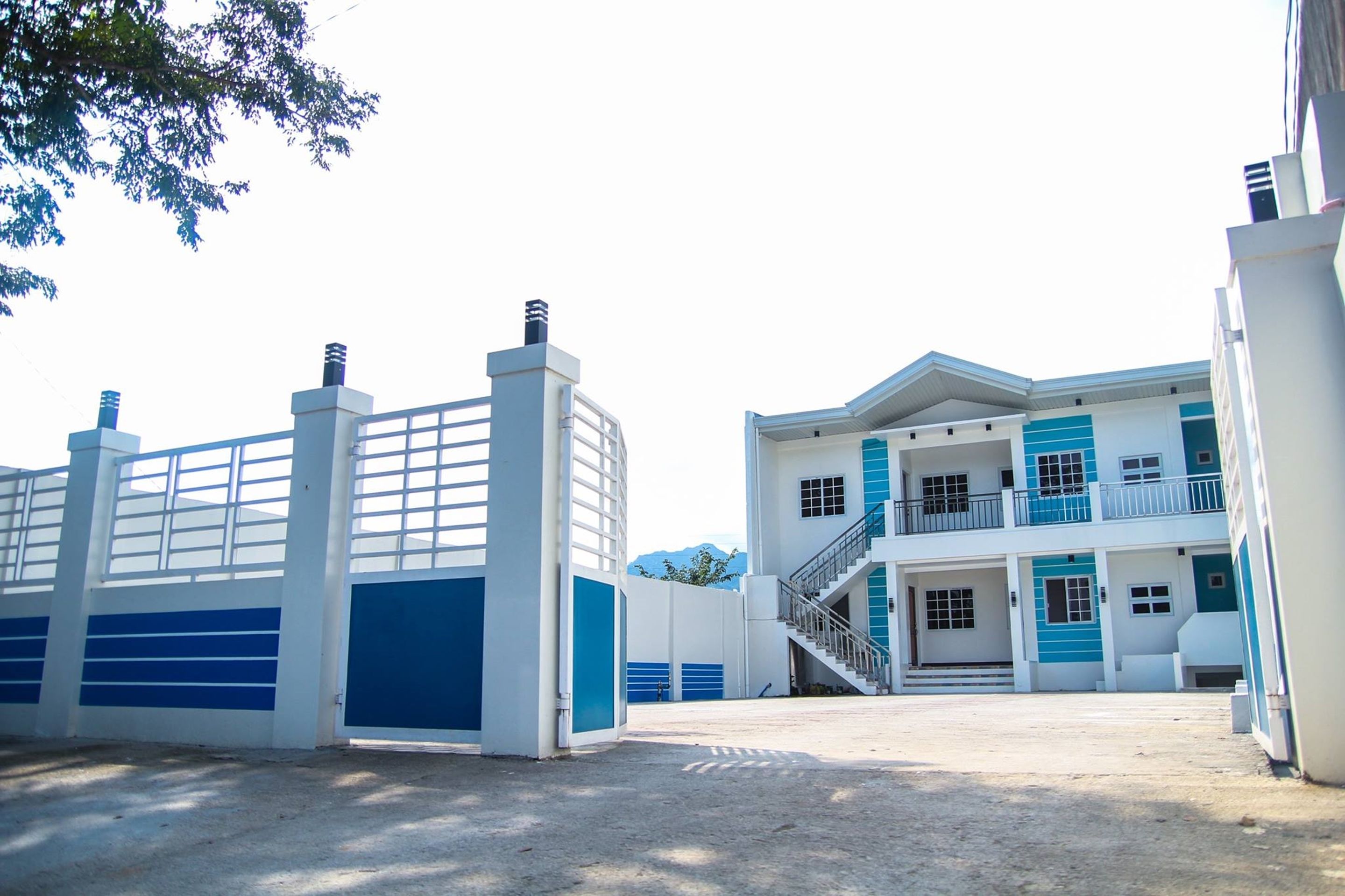 Um edifício de dois andares com esquema de cores azul e branco, entrada com portão e escadaria que leva ao andar superior.