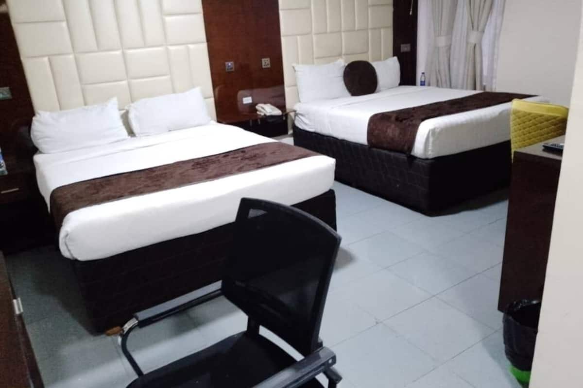 Duas camas de casal com cabeceiras, uma cadeira preta e uma pequena mesa num quarto de hotel.