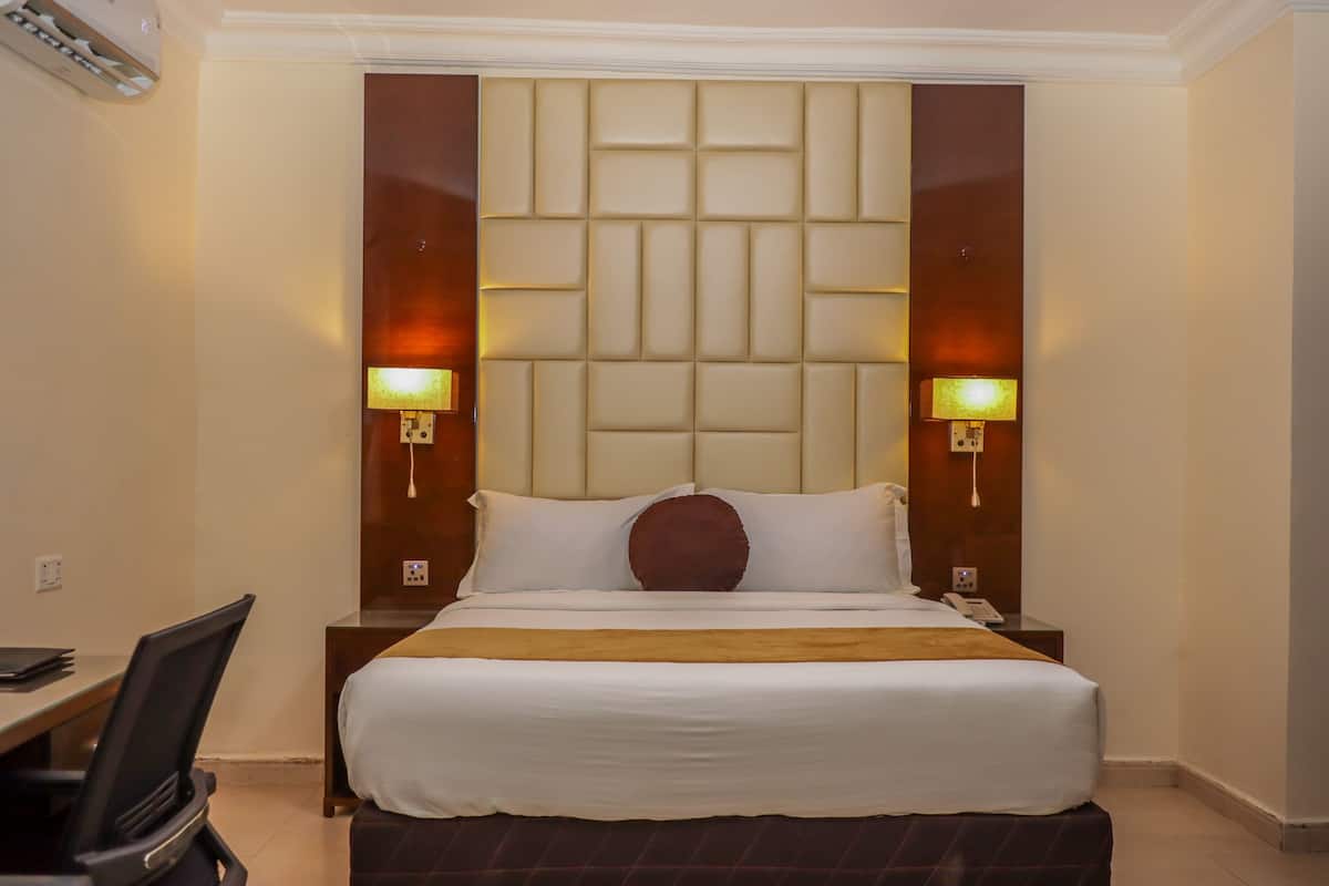 Quarto de hotel com uma cama grande, duas luminárias de cabeceira, uma escrivaninha com cadeira e ar condicionado fixado na parede.