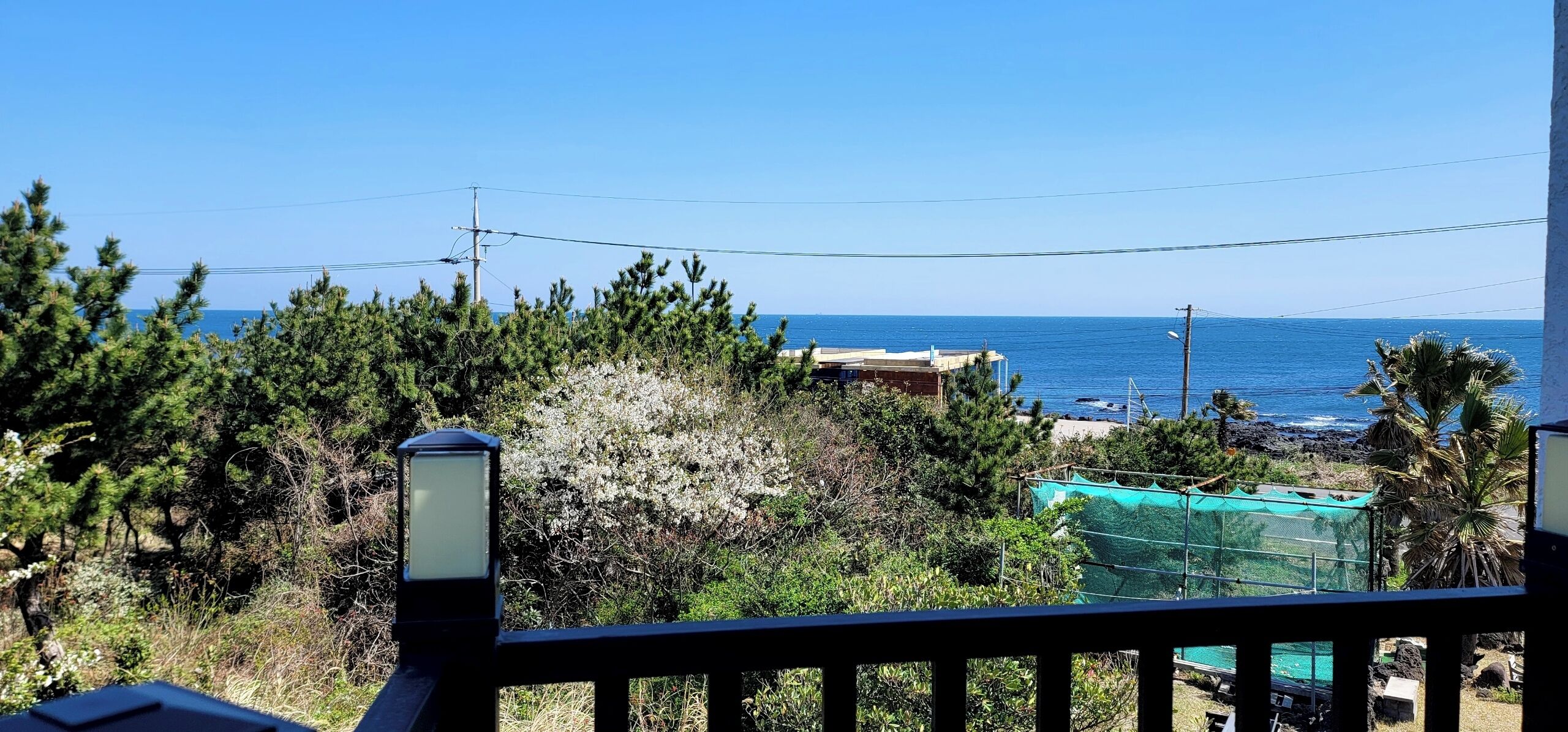 Vista costeira de varanda com guarda, sobre o mar e um edifício com telhado verde.
