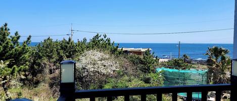 Vista costeira de varanda com guarda, sobre o mar e um edifício com telhado verde.