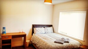 Quarto com cama, escrivaninha e janela.