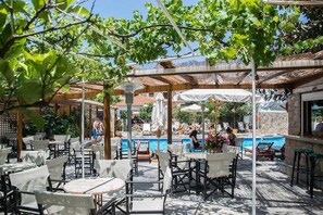 Uma área de varanda externa com mesas, cadeiras, piscina e guarda-sóis.