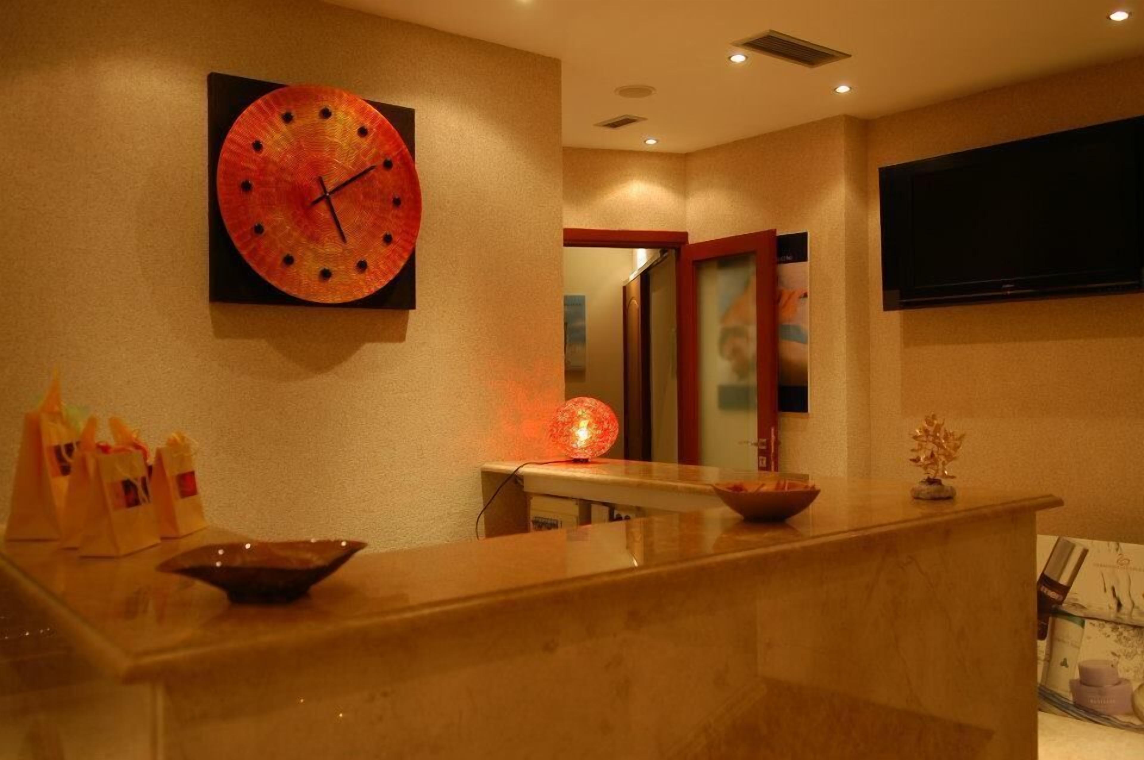 Uma área de recepção de hotel com um relógio de parede grande, uma televisão e um balcão de atendimento.