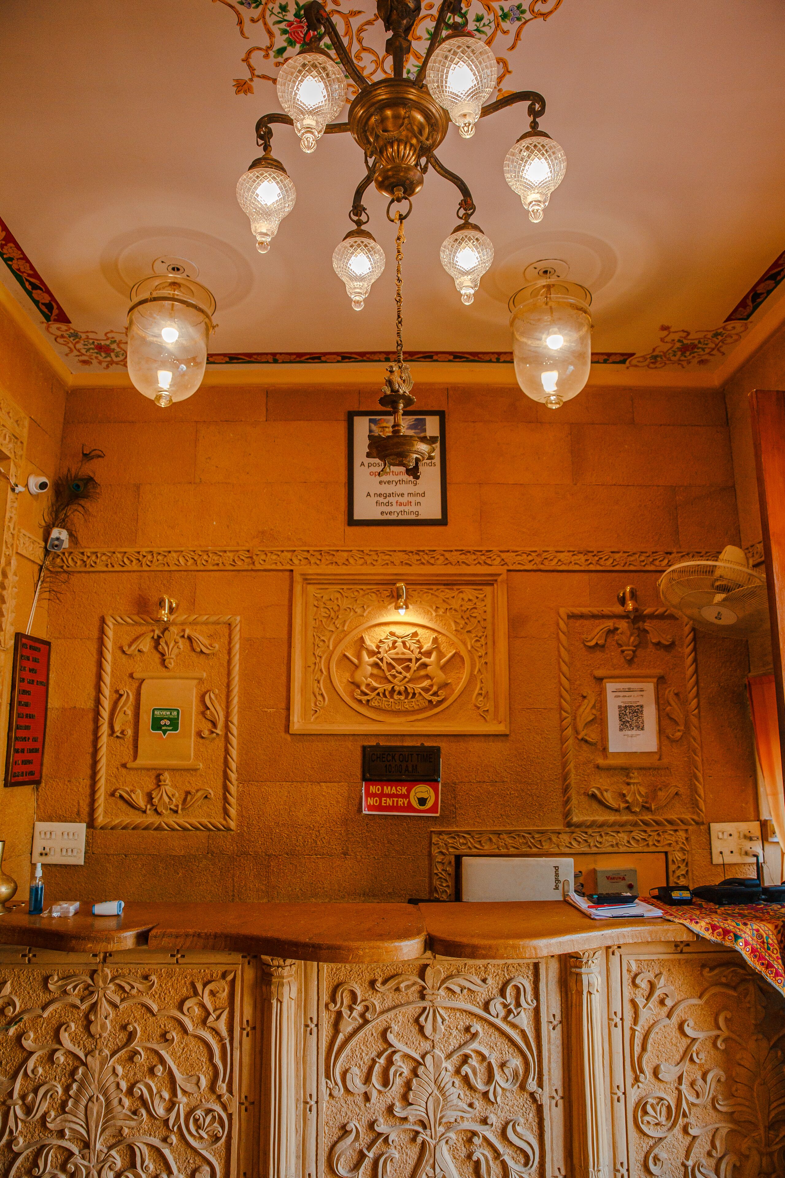 Uma área de recepção com um candelabro, decorações elaboradas nas paredes e um balcão com uma placa.