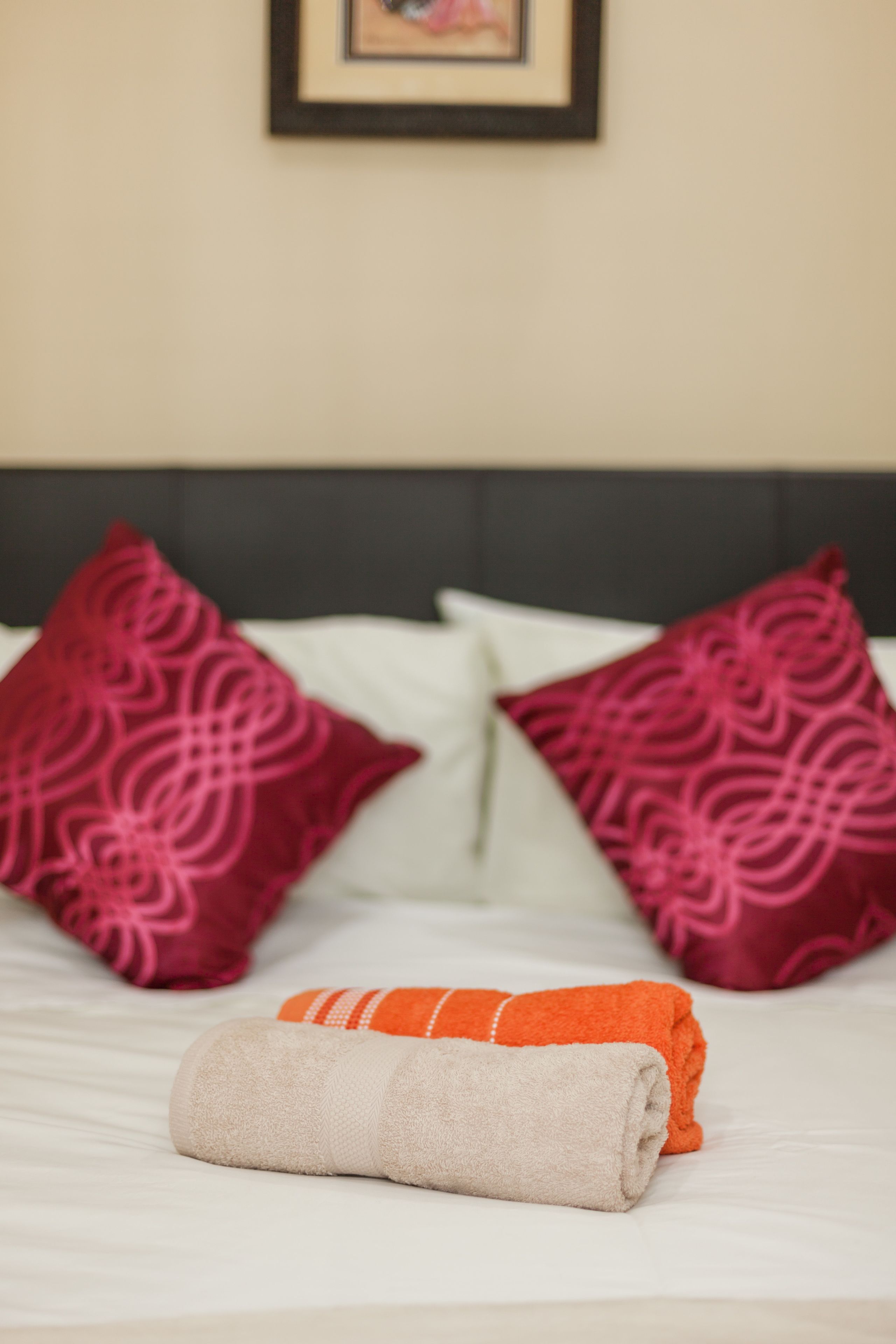 Cama bem arrumada com duas almofadas decorativas e uma toalha enrolada.