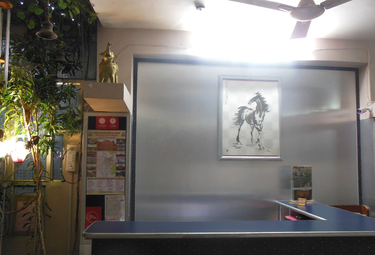 Uma área de recepção com um balcão, uma pintura emoldurada de cavalos, um mural de avisos e um ventilador de teto.