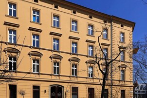 Um edifício com vários andares, fachada simétrica, janelas uniformemente distribuídas e uma entrada central com arco decorativo.
