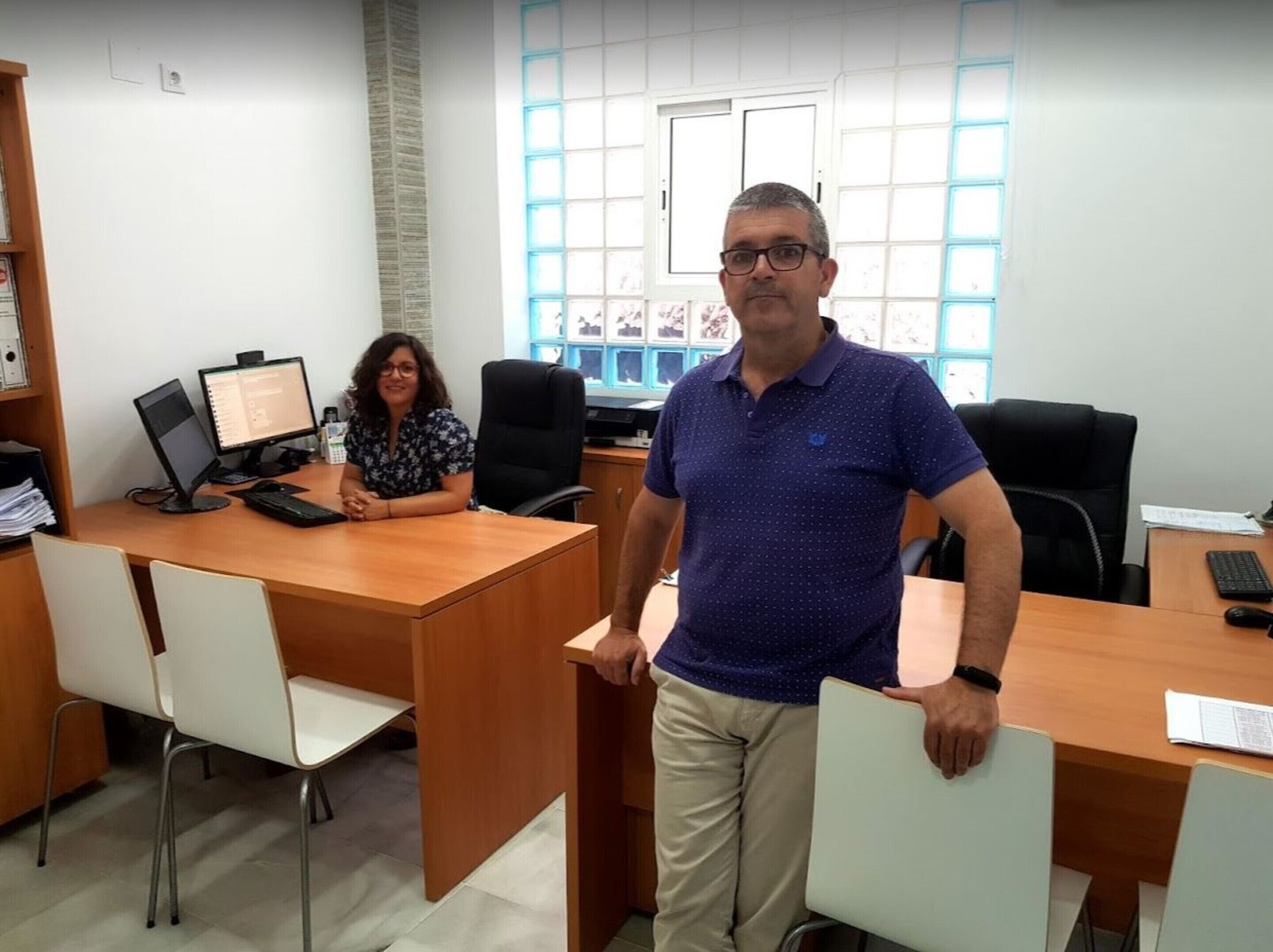 Uma sala de conferências com uma mesa de madeira, duas cadeiras, um computador e uma janela com persianas.