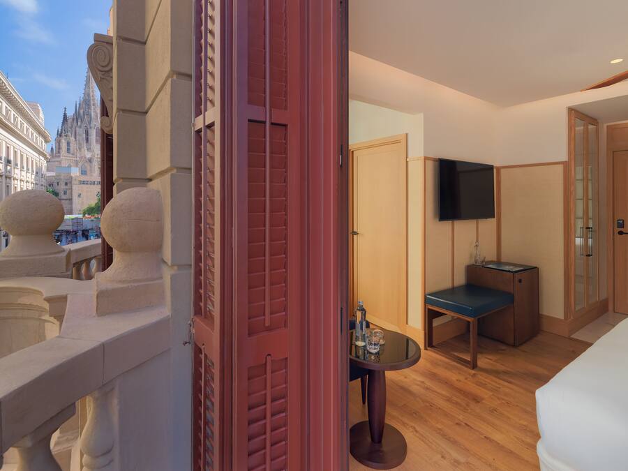 Quarto de hotel com varanda, televisão, mesa pequena e cama.