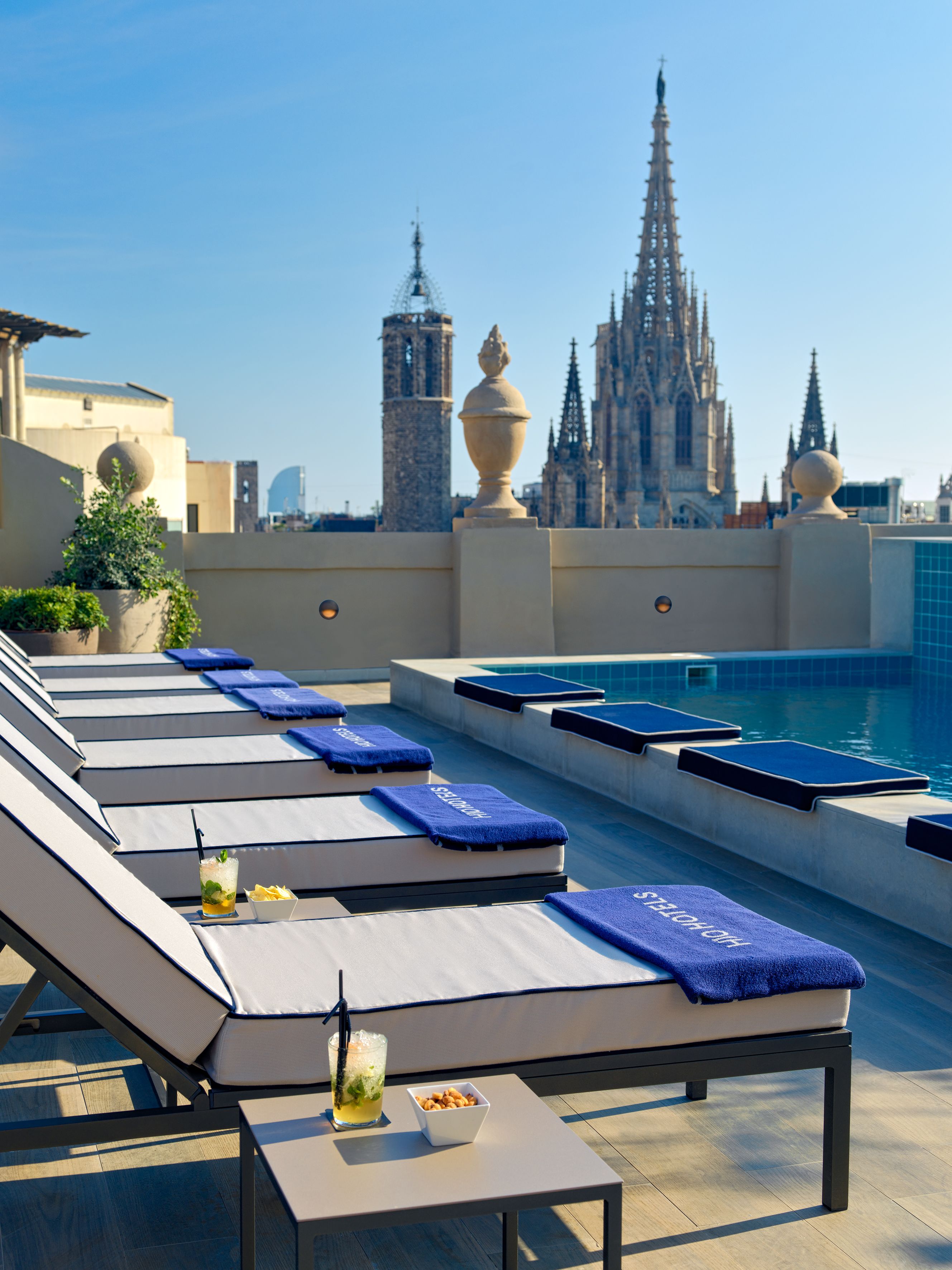 Área de piscina no terraço, com espreguiçadeiras e vista para uma catedral.