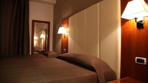 Quarto de hotel com uma cama grande, duas luminárias de cabeceira, uma mesinha de madeira e um espelho na parede.