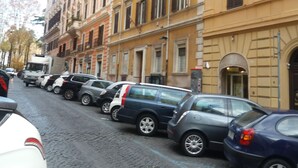 Rua com carros estacionados e edifícios históricos amarelos, com várias janelas e persianas.